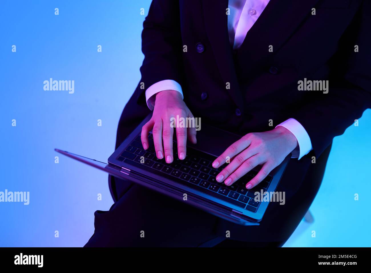 Business woman working, typing on laptop over blue background in neon ...