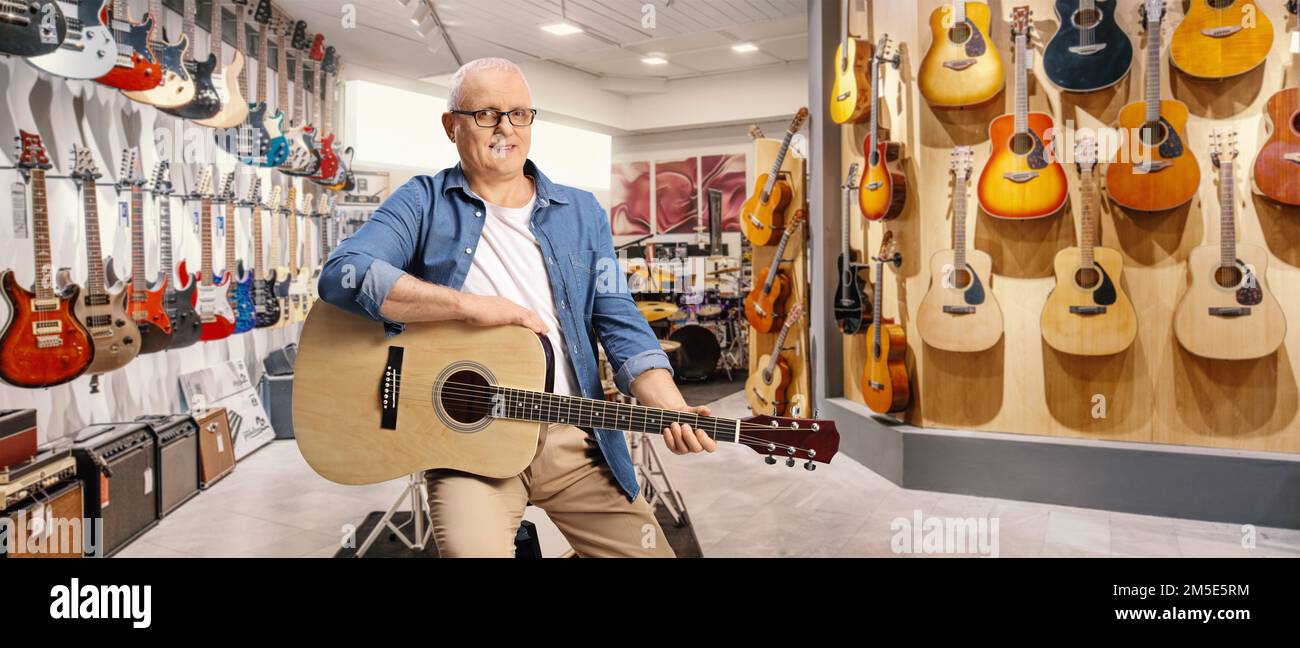 Mature man sitting on a chair with an acoustic guitar inside a music ...