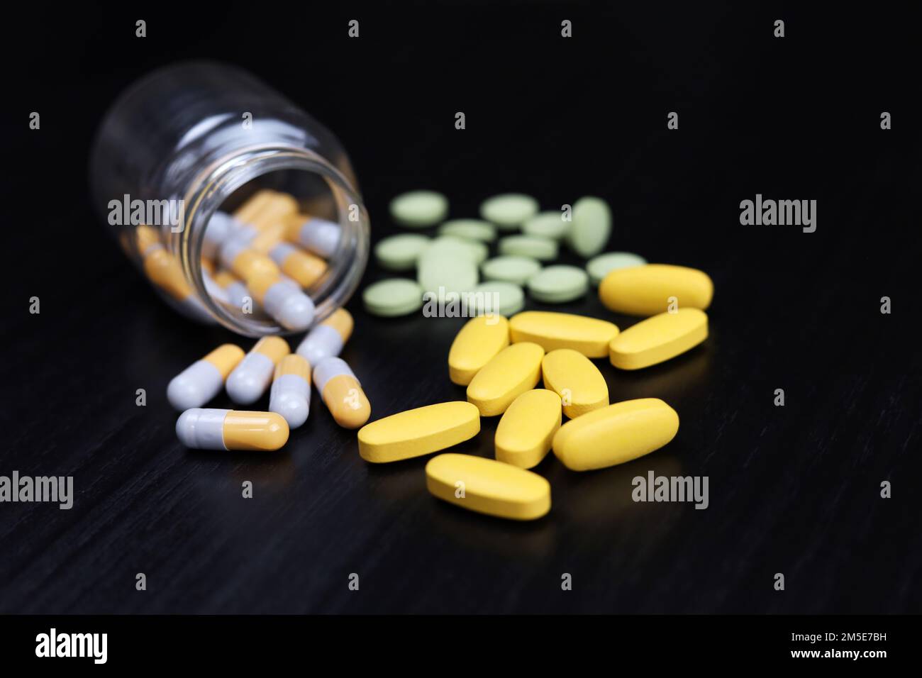 Different pills on a black wooden table, variation of medication in ...