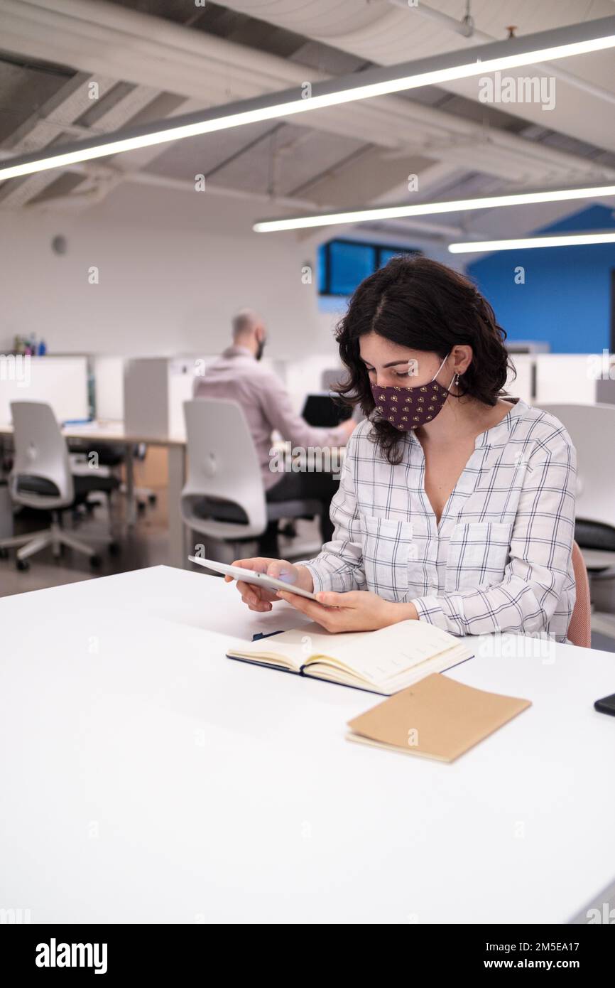 Two young colleagues in masks sitting in the office and working Stock ...