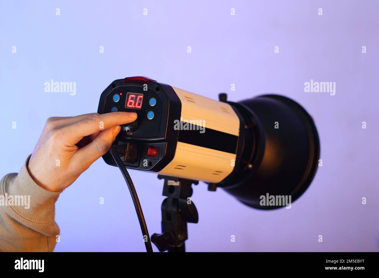 a person adjusting a studio flash on the back panel against a blue wall ...