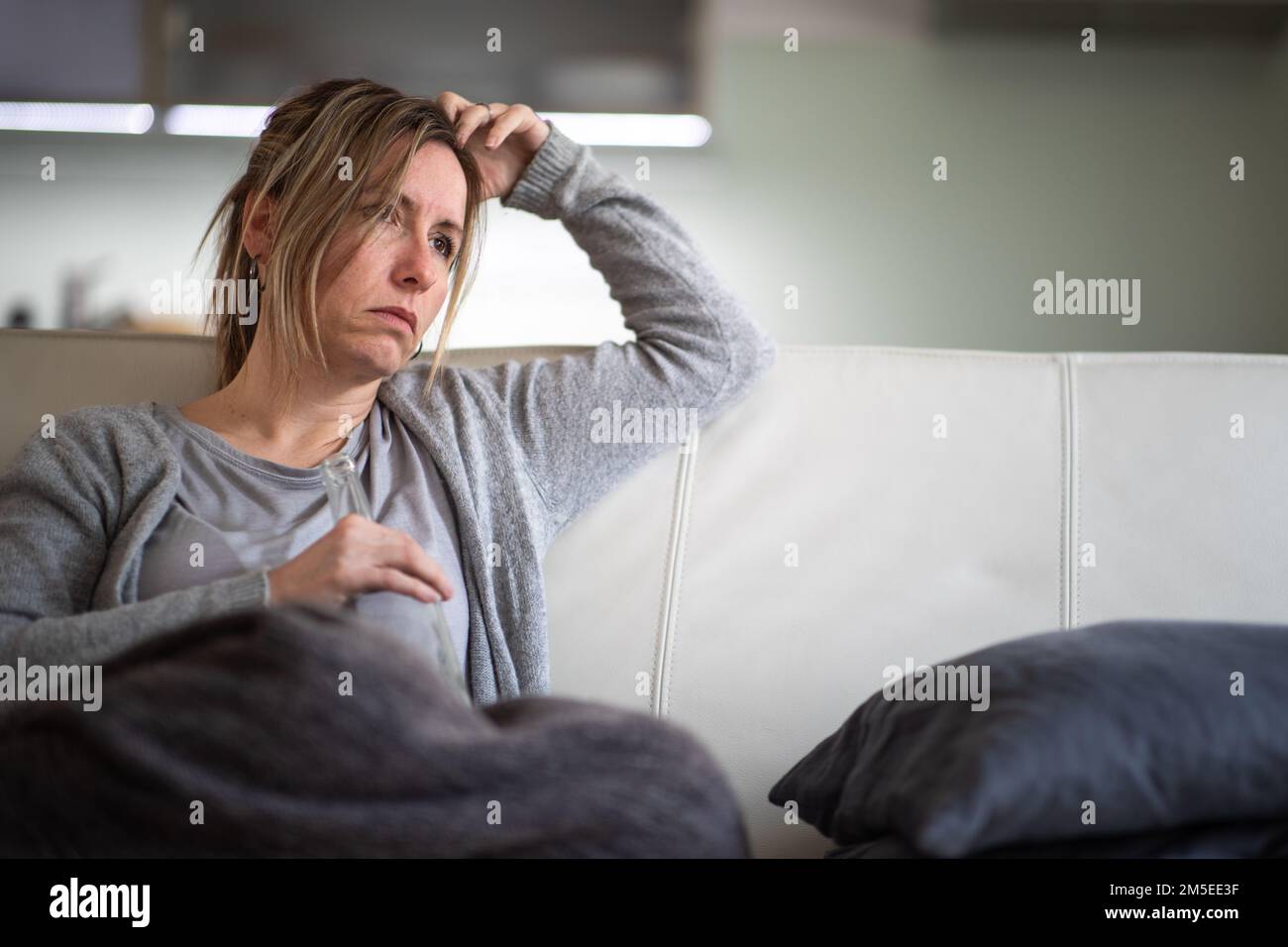 Midlle aged woman at home with a bottle of strong alcohol in her hands ...