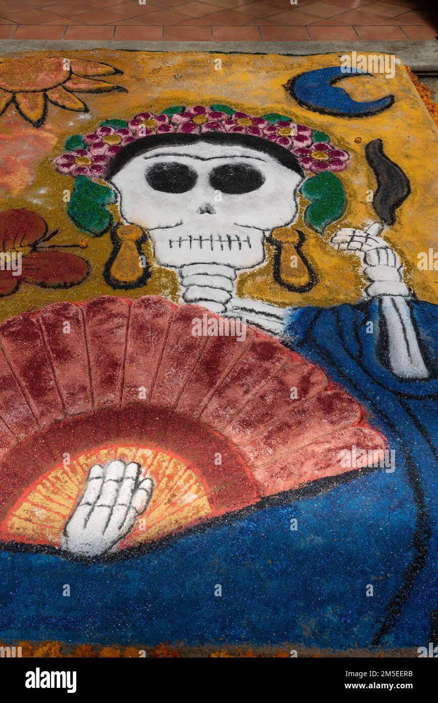 A colorful sand painting of La Catrina in front of an ofrenda to ...
