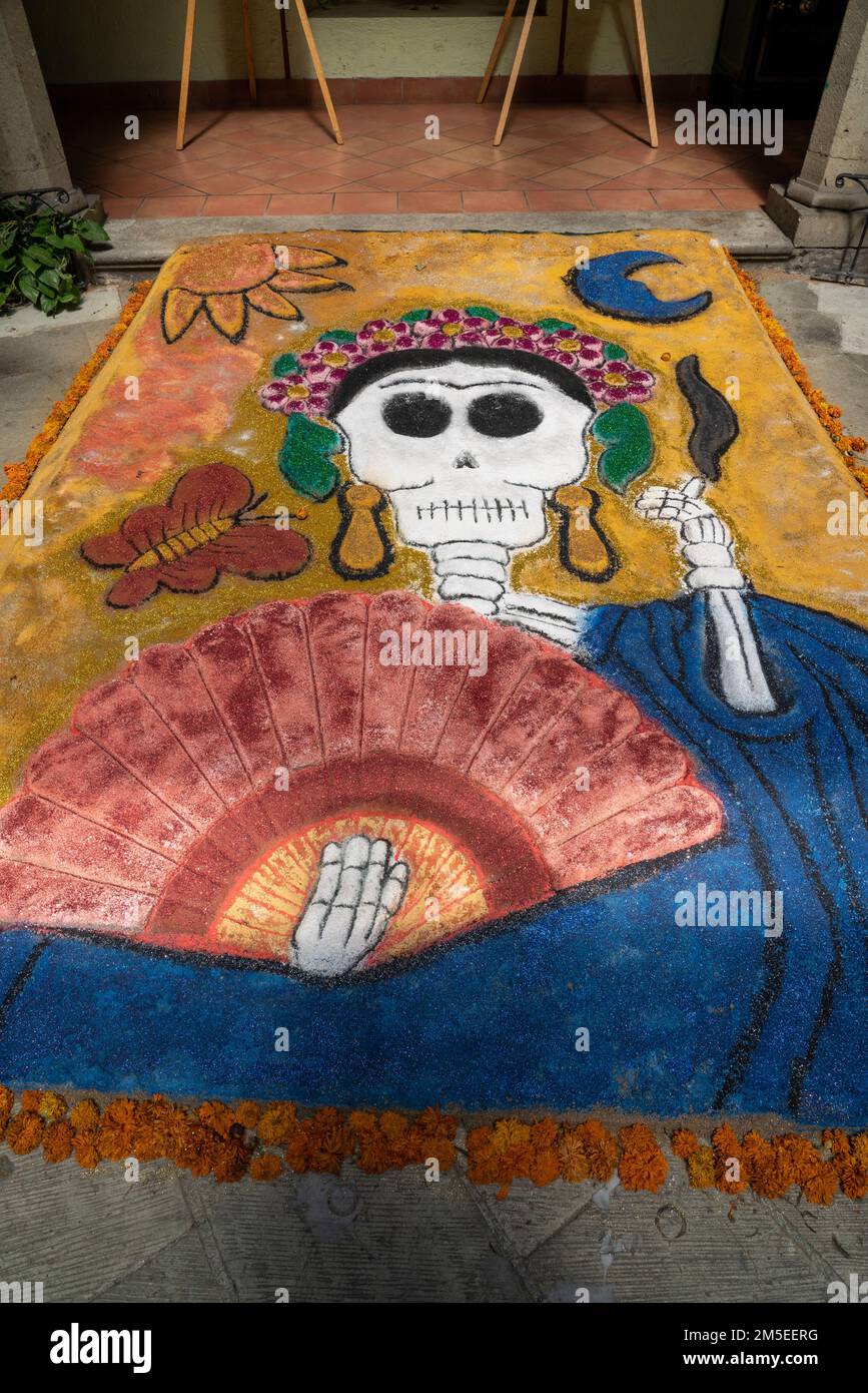 A colorful sand painting of La Catrina in front of an ofrenda to ...