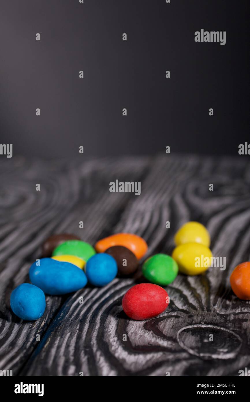 Chocolate candy in multi-colored glaze. Scattered on black pine boards ...