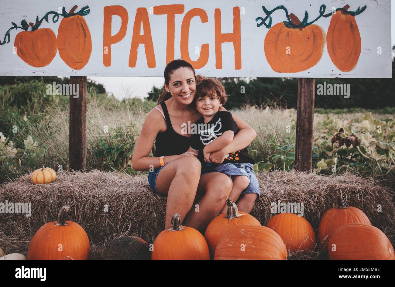 A young mom with her son sitting on a hale bale at a Pumpkin patch in ...
