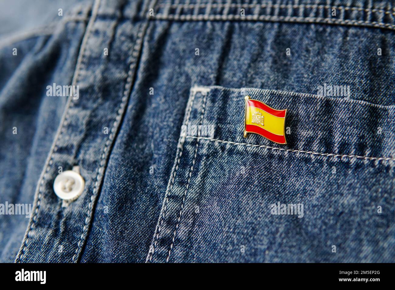 Metal badge with the flag of Spain is pinned on blue jeans jacket ...