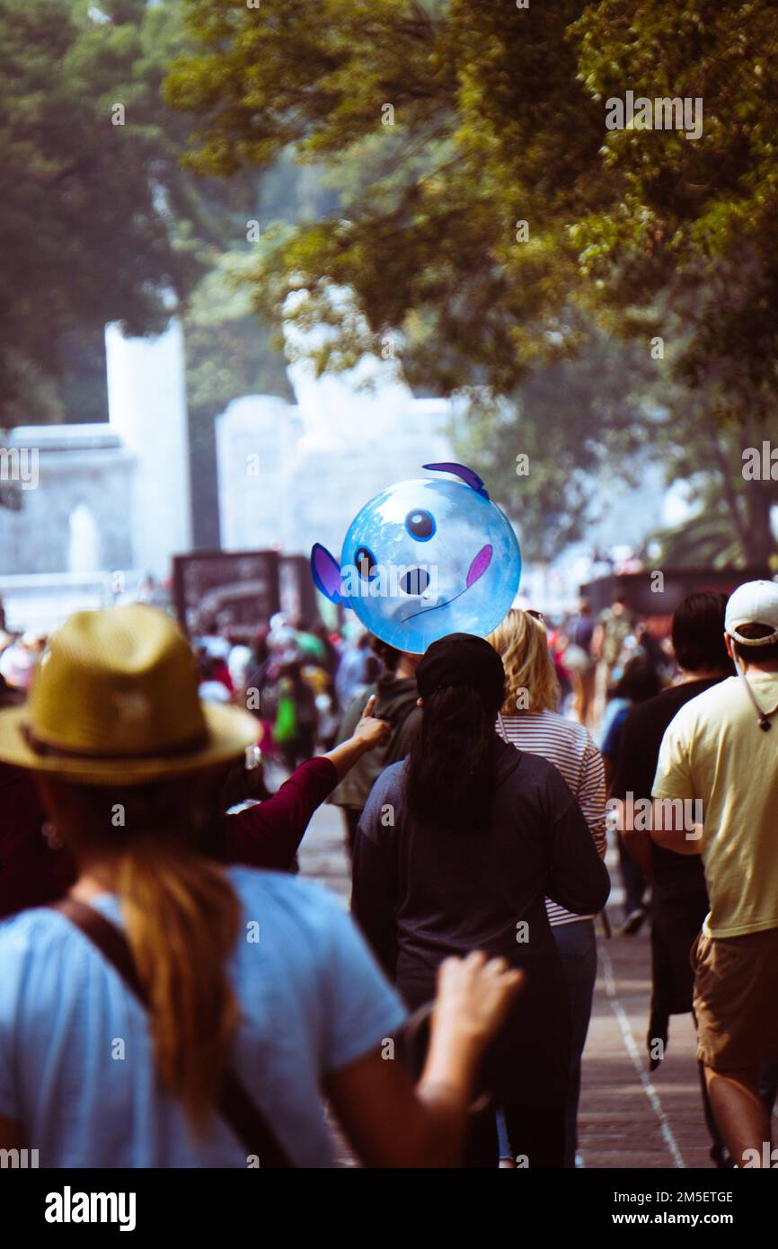 A vertical back view of a female holding a blue balloon walking on a ...