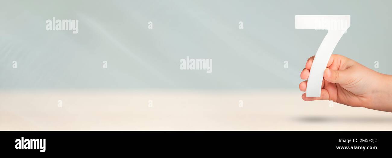 Number seven in hand. Hand holding white number 7 on blurred background ...