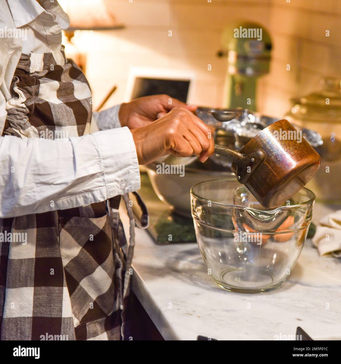 woman preparing food pouring ingredients from a small copper pot into a ...