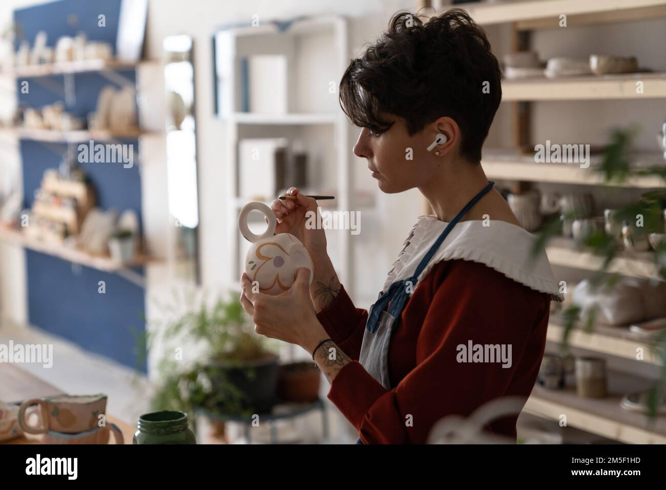 Concentrated Italian woman artist using brush applies paint on handmade ...