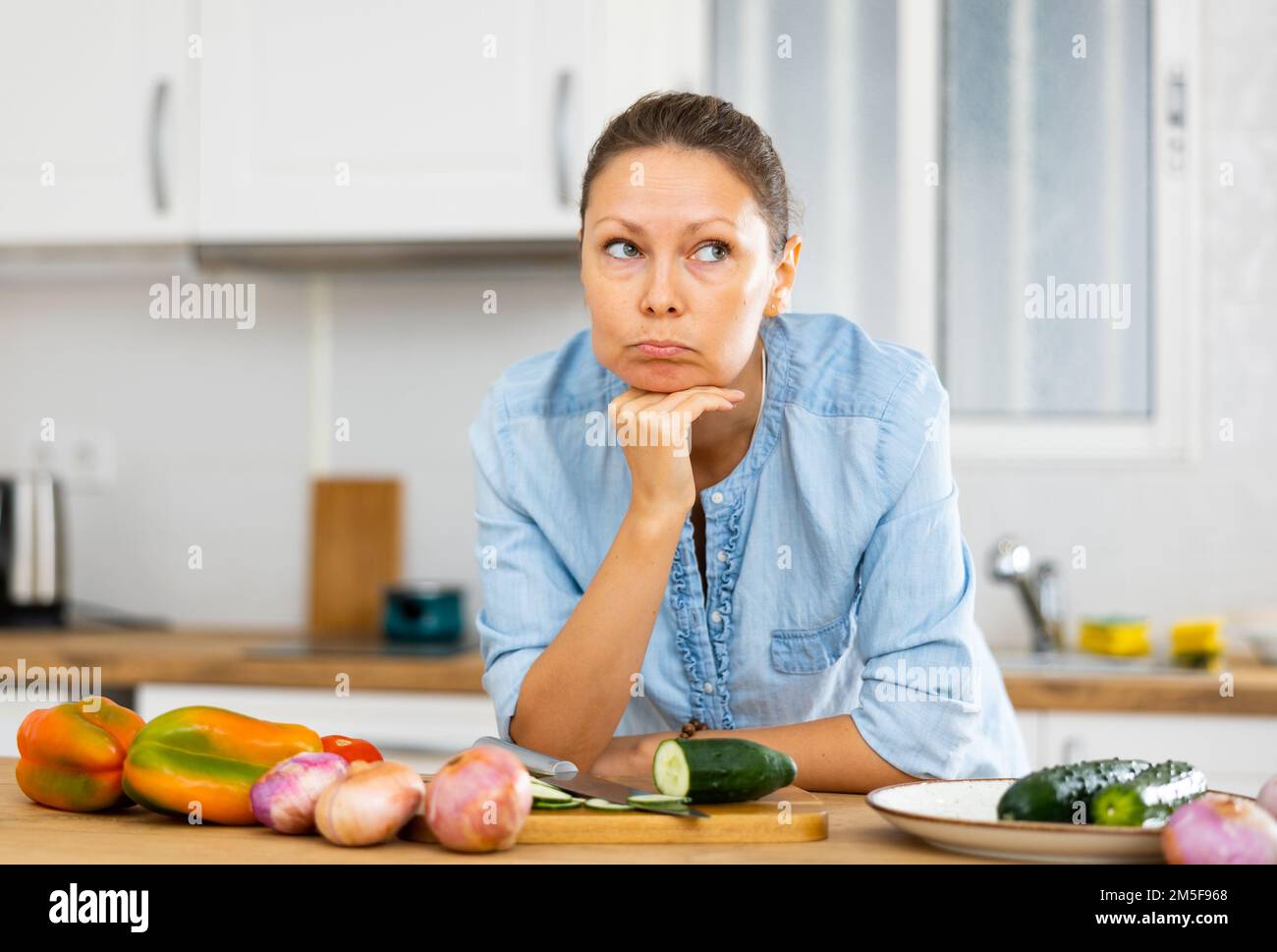 Sad young adult woman standing in kitchen Stock Photo - Alamy