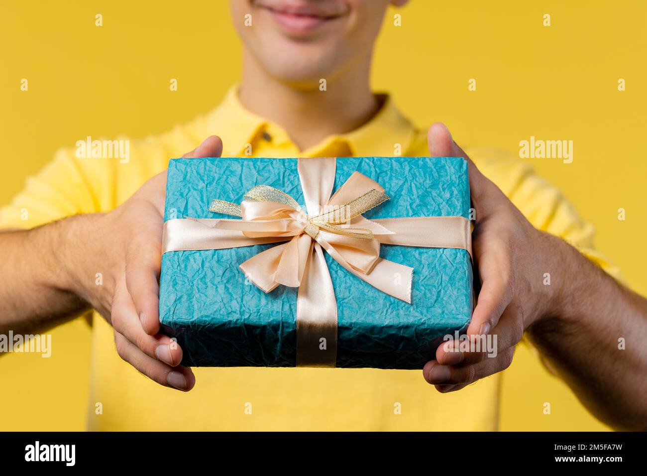 Man gives gift box by hands to camera on yellow background. Guy smiling ...