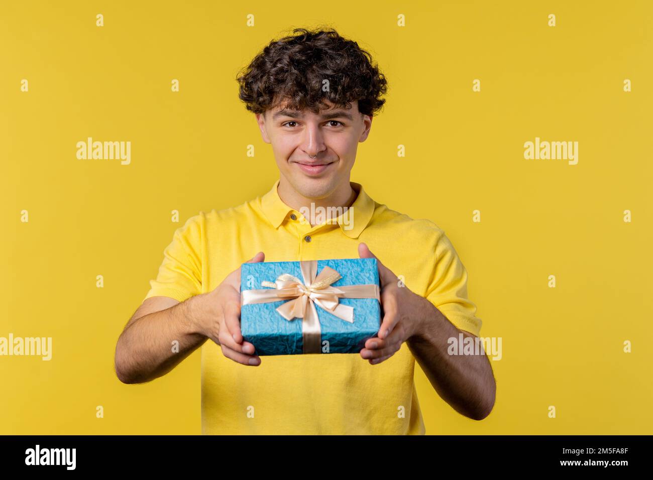 Man gives gift box by hands to camera on yellow background. Guy smiling ...