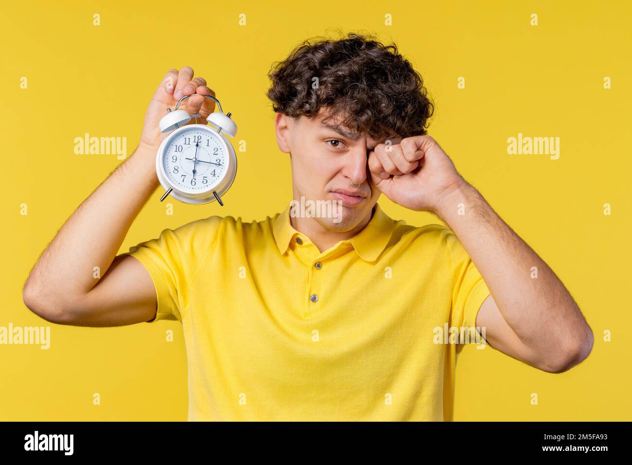 Woken up by alarm clock sleepy man holding it in hand. Yellow ...