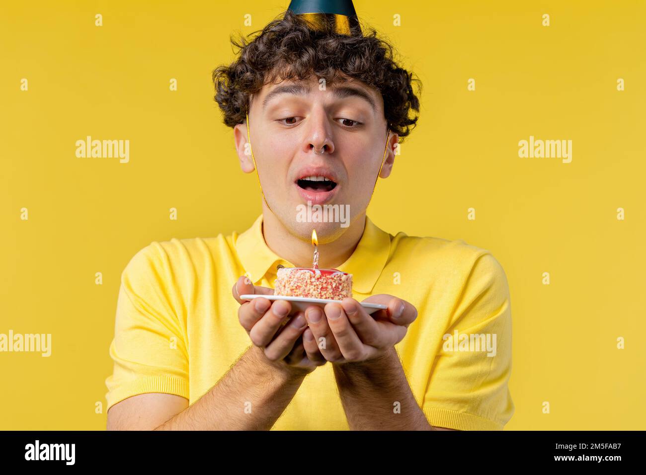 Happy birthday man making wish - blowing candle on cake. Curly haired ...