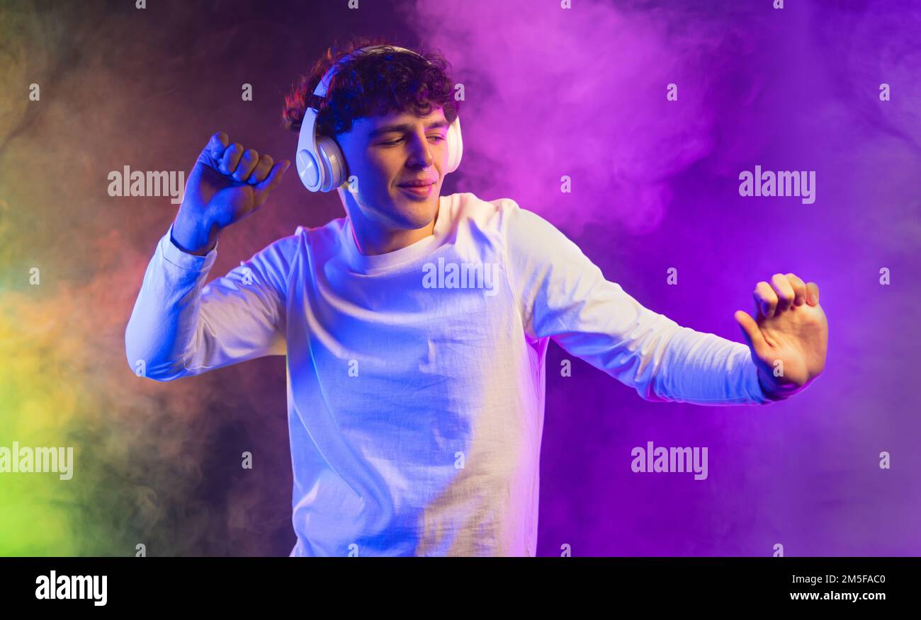 Positive man listening music with headphones, dancing on dark neon ...