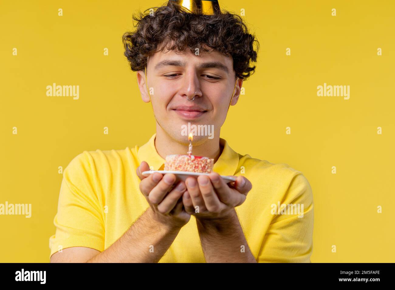 Happy birthday man making wish - blowing candle on cake. Curly haired ...