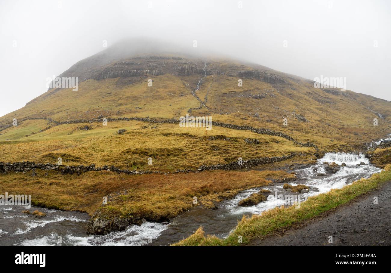 A waterfall crossing the yellow grass fields below the mountain Stock ...