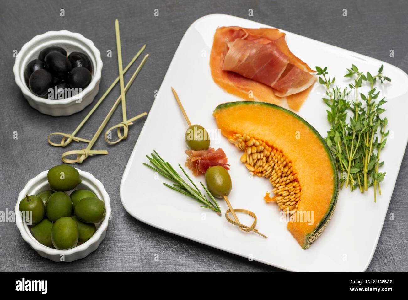 Two green olives and jamon on skewer. Slice of melon and sprigs of ...