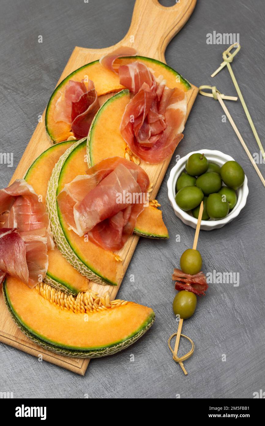 Jamon on slice of melon on cutting board. Two green olives and jamon on ...