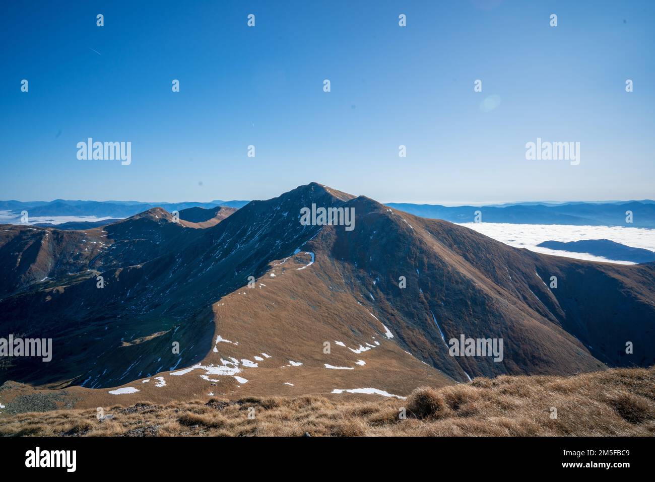 A peak of a rocky mountain partly covered with snow with blue sky in ...