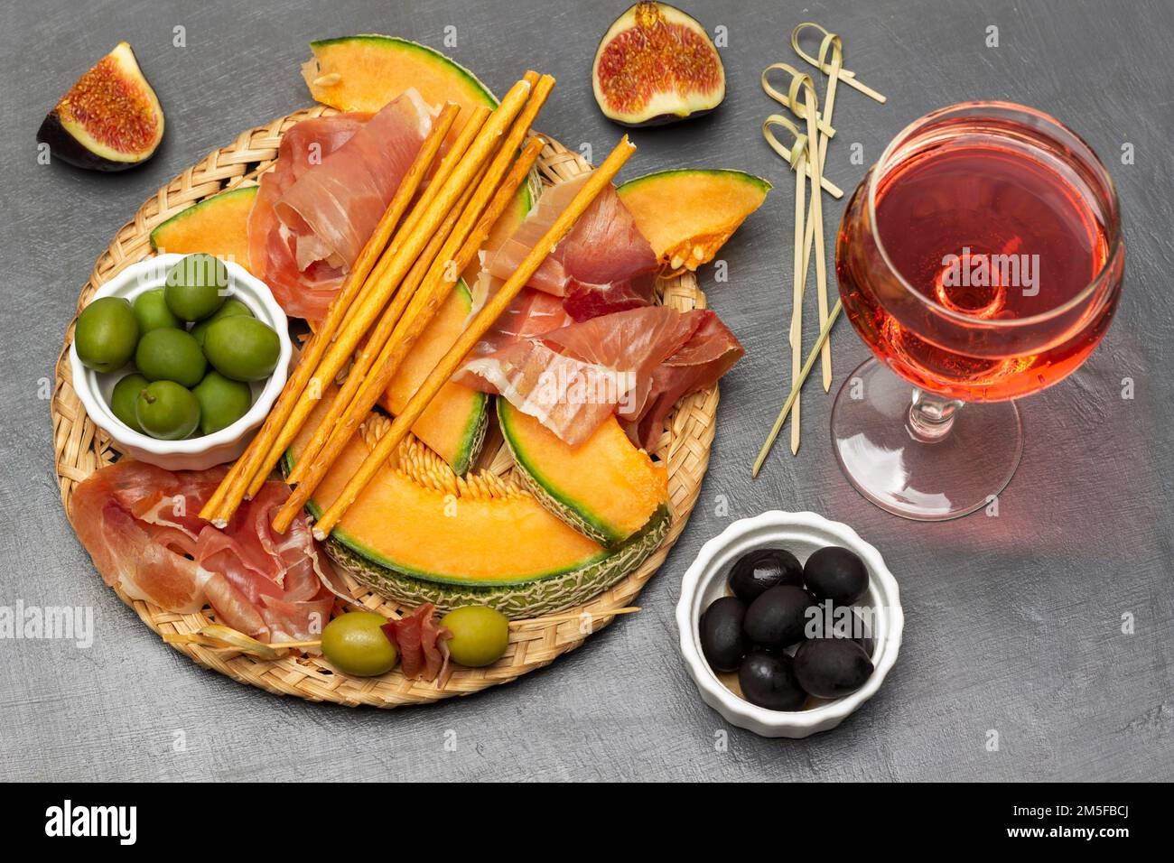 Melon, jamon, green olives on a wicker plate. Glass with rose wine and ...