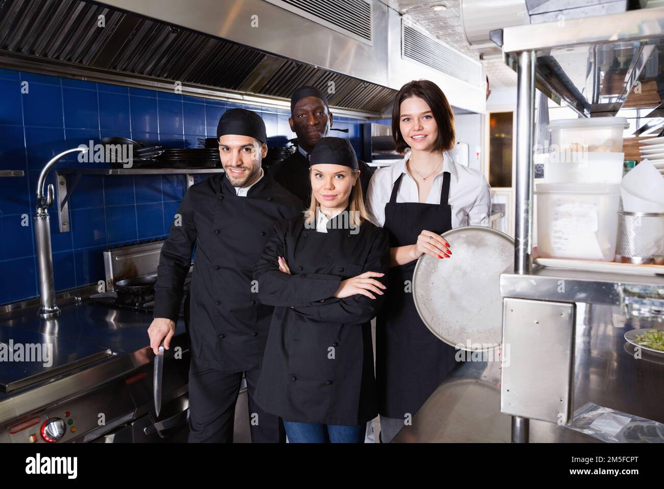 Woman waiter with command of cooks are posing together on kitchen in ...