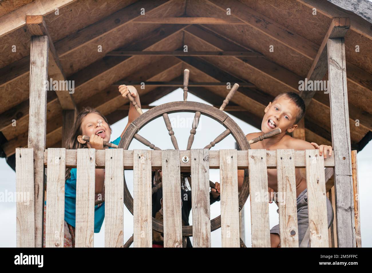 Cheerful little girl and boy fool and make faces steering ship wheel ...