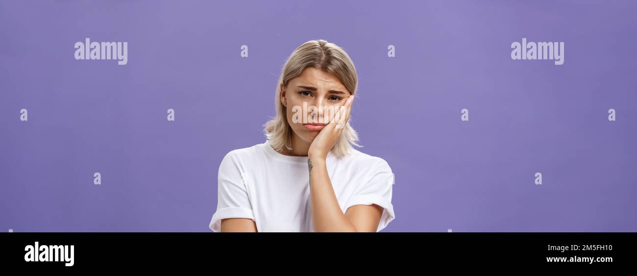 Waist-up shot of unhappy miserable and sad cute blonde female in white ...