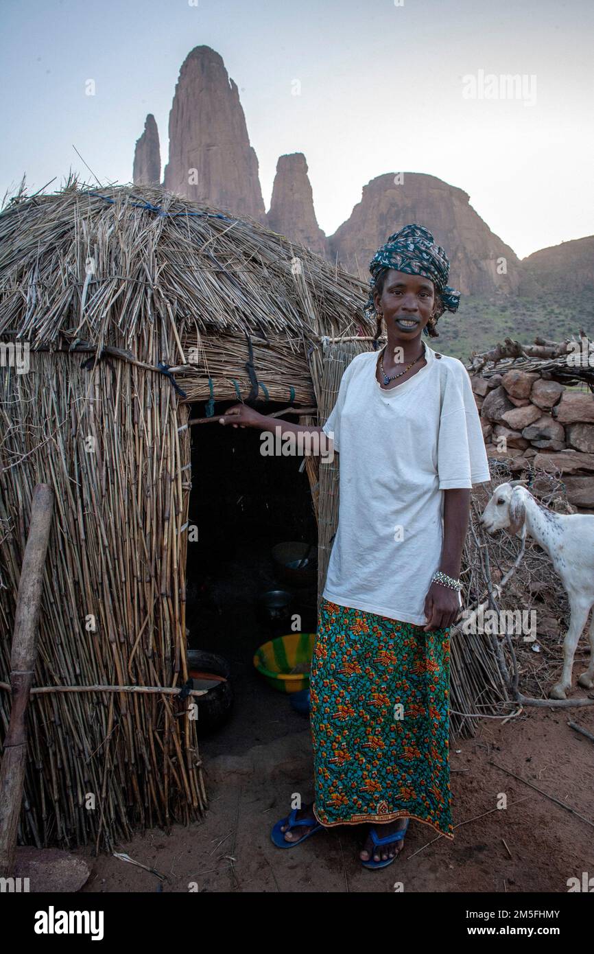 Peul woman in front of straw hut with background view of the Monument ...