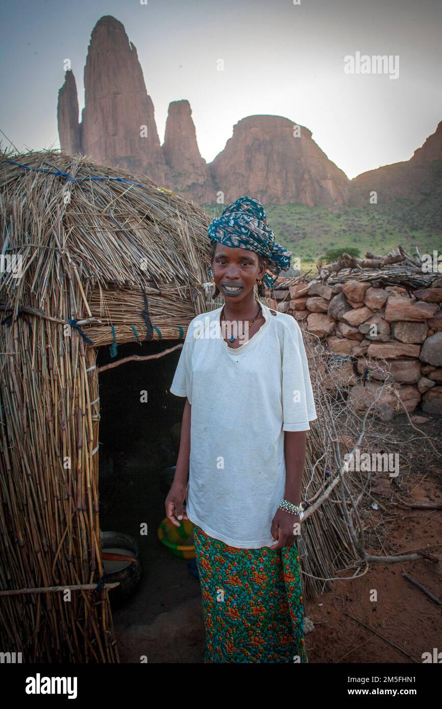 Peul woman in front of straw hut with background view of the Monument ...