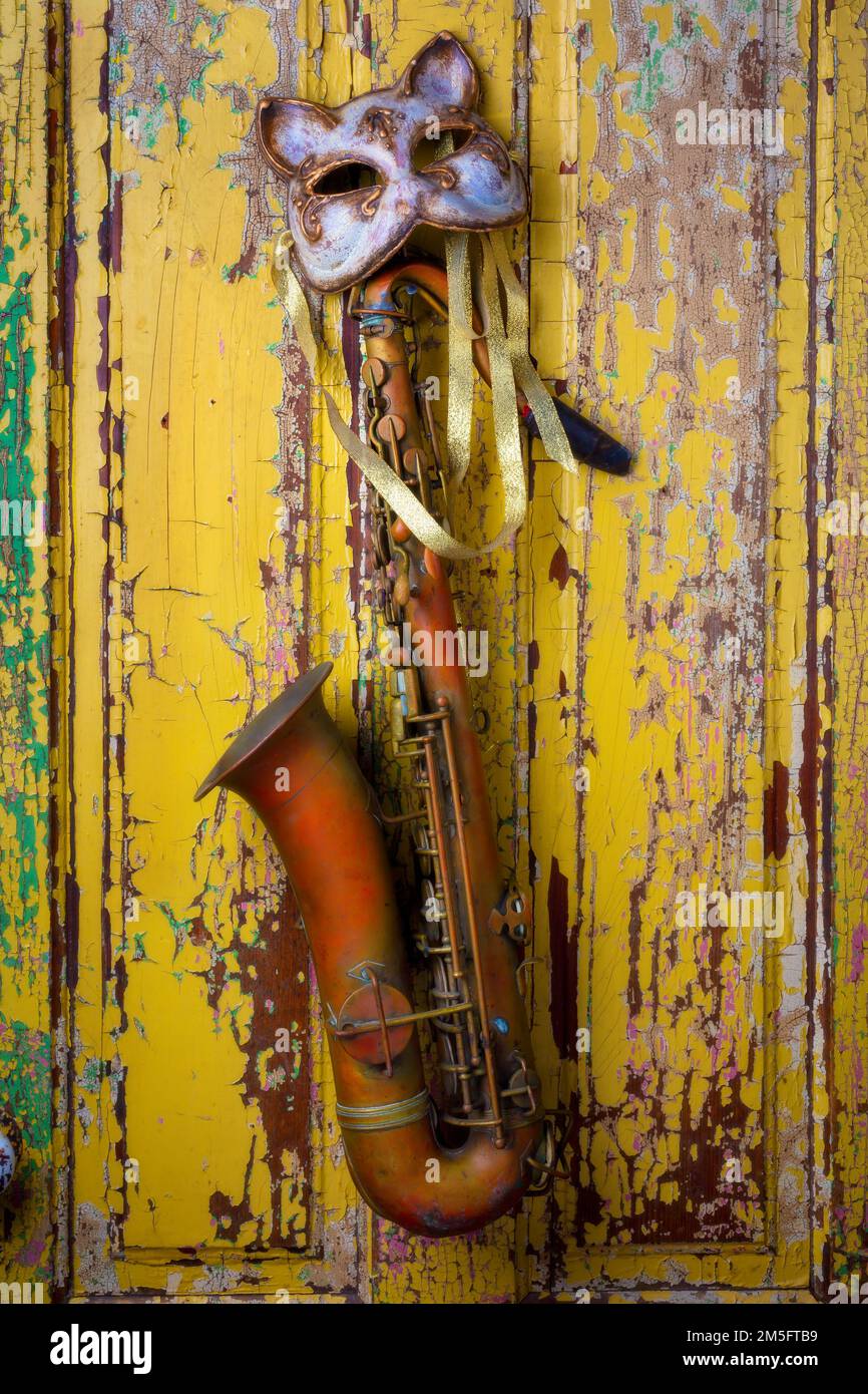 Cat mask and old saxophone hanging on old weathered yellow door still ...