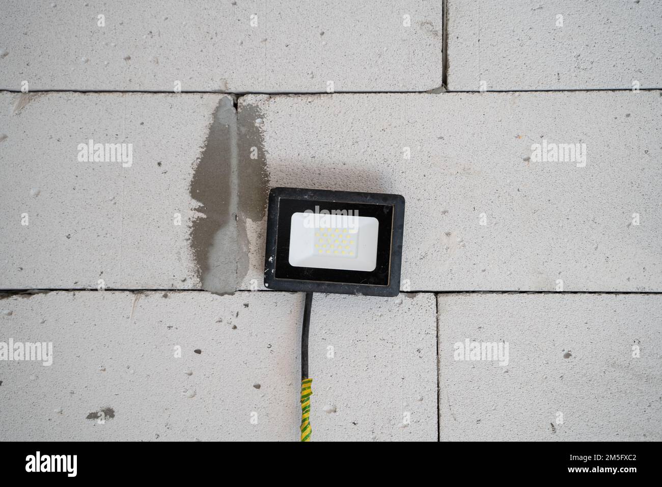 A small construction LED spotlight hangs on an aerated concrete wall ...