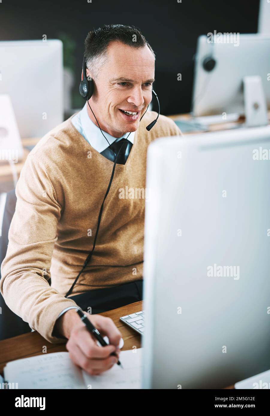 Hes happy to help. a handsome mature male operator working at his desk ...