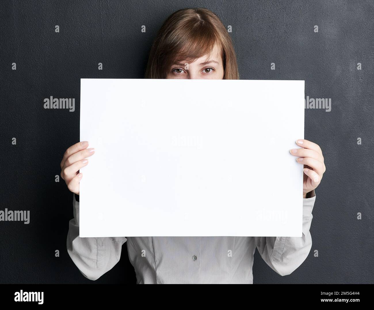 She has something to say. a woman holding a blank board against a dark ...