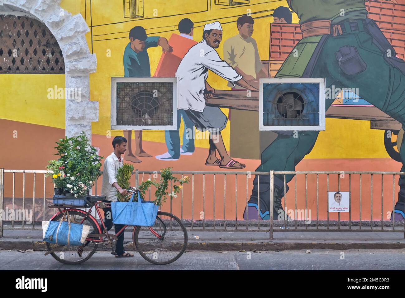 A cyclist transporting garden plants passes a colorful wall painting at ...