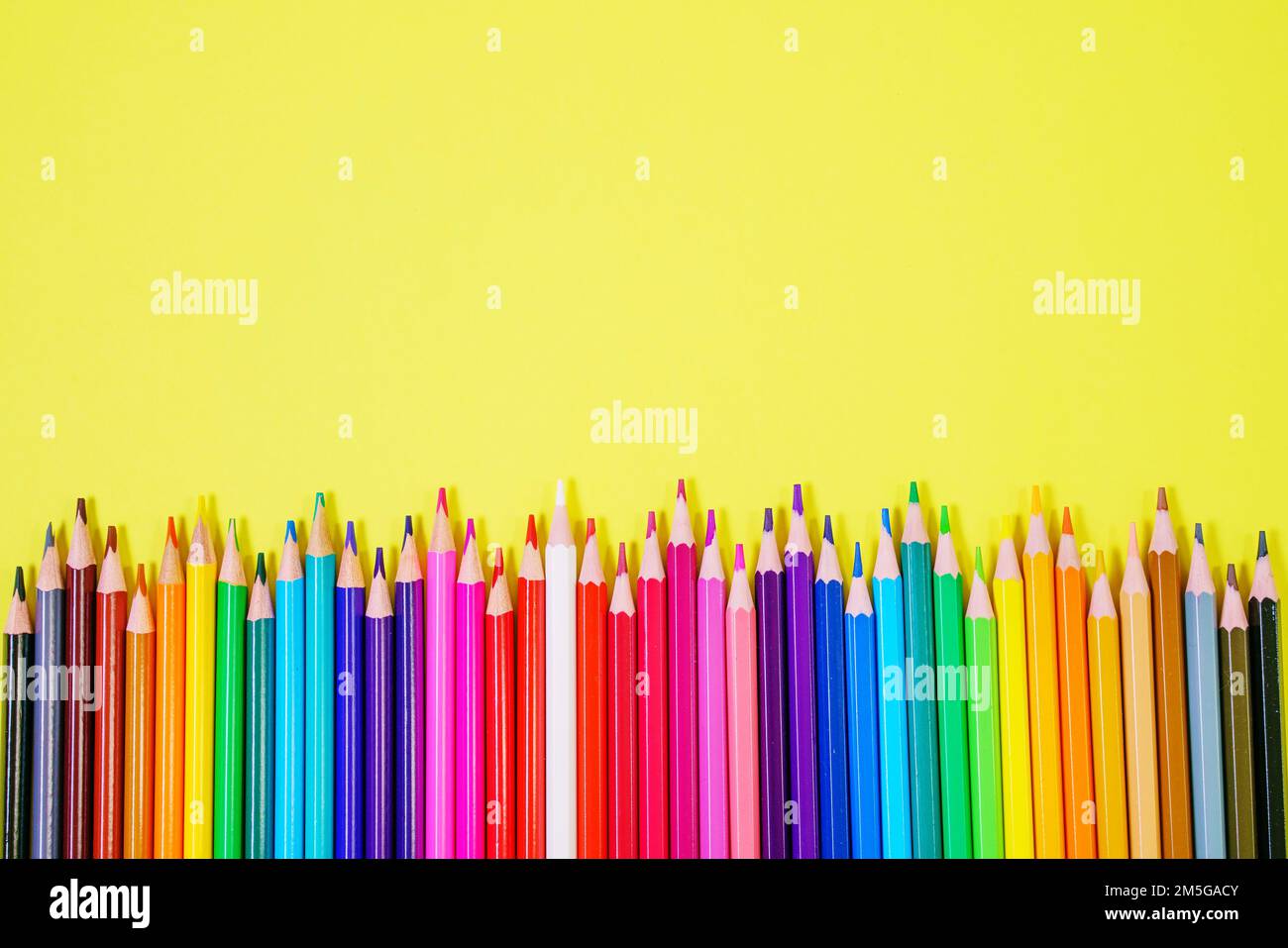 Assortment of colored pencils in various iridescent colors on a yellow ...