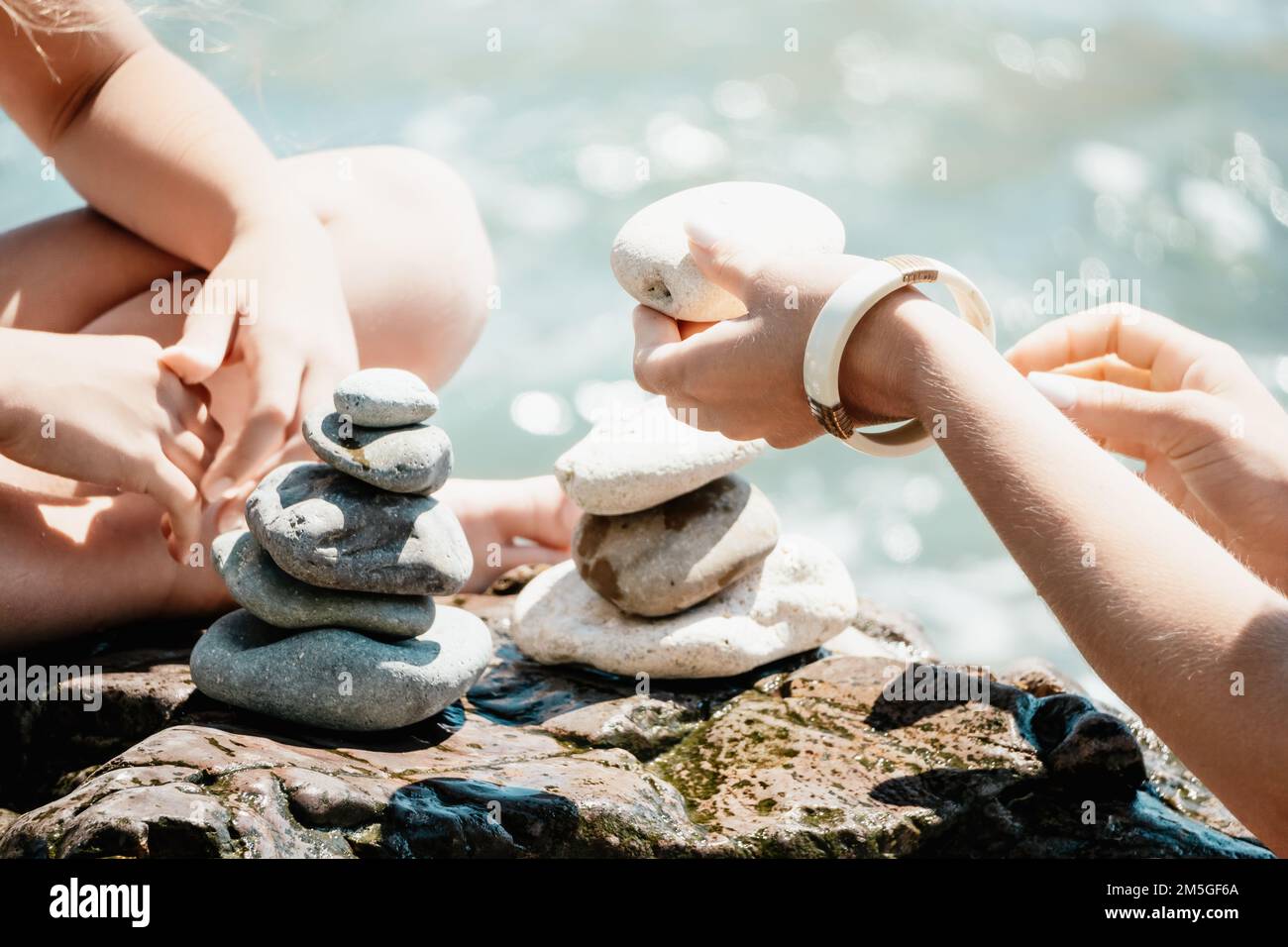 Woman with daughter bilds stones pyramid on seashore on a sunny day on ...