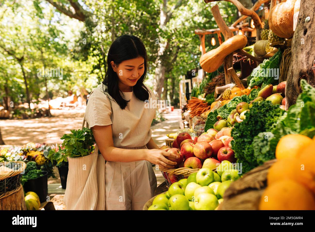 Smiling Asian woman choosing fruits. Female with a shopping bag at an ...