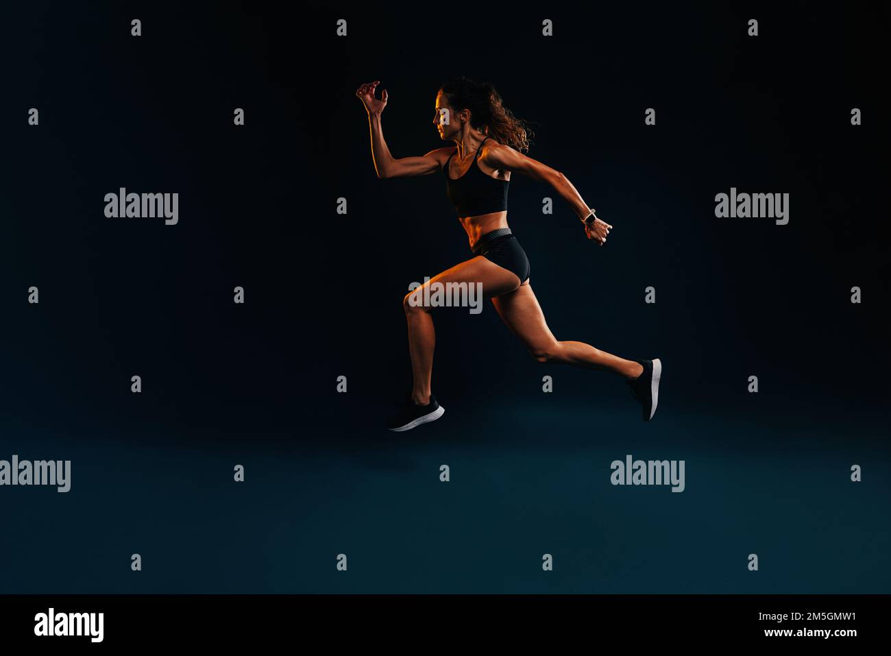 Sprinter against a black background. Muscular female running and ...