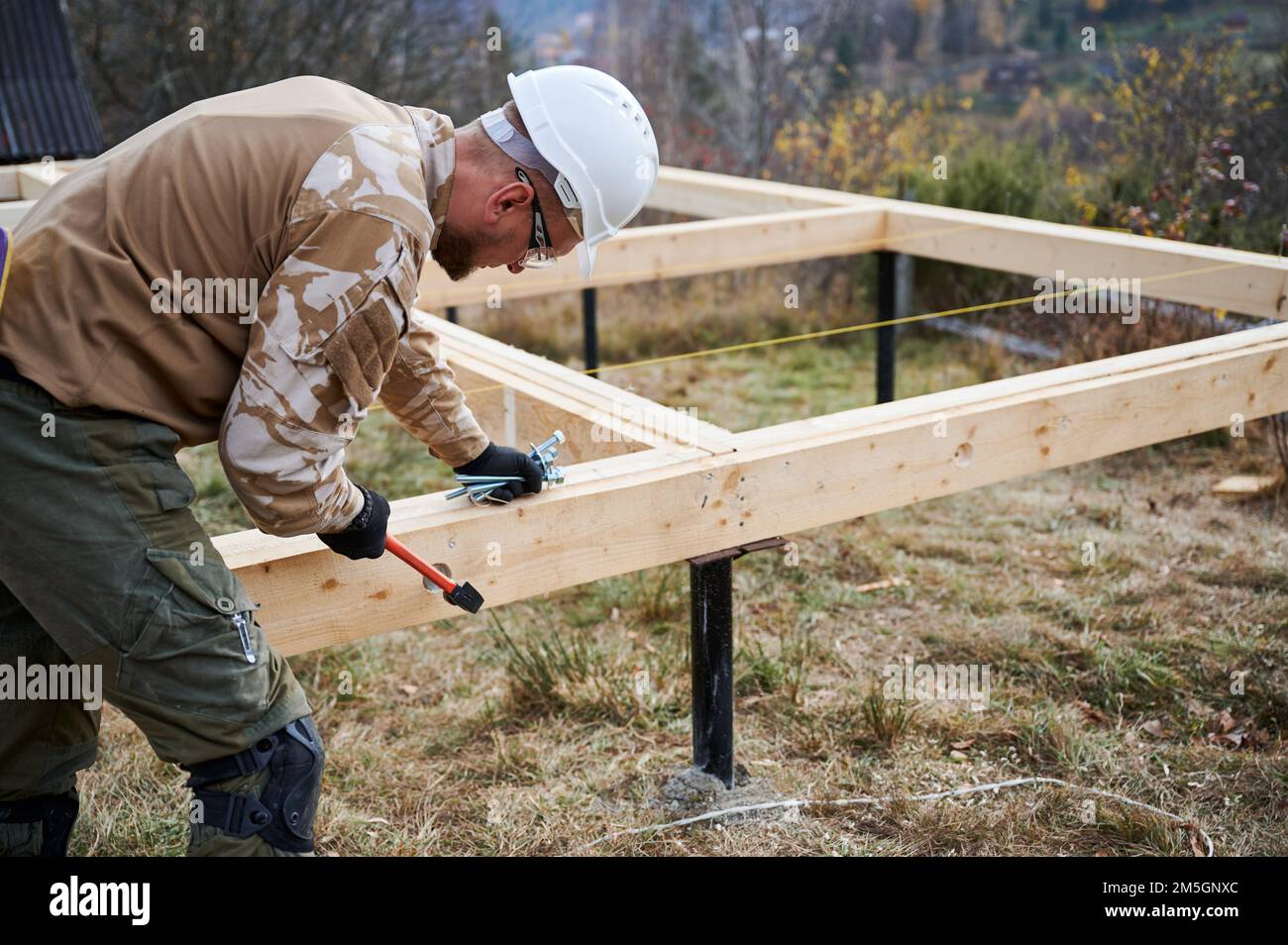 Man worker building wooden frame house on pile foundation. Carpenter ...