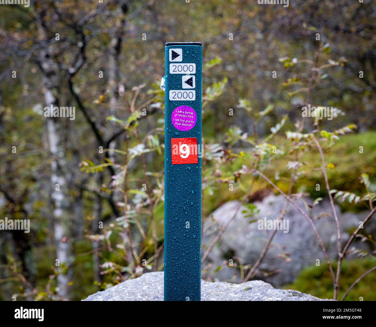 An old blue sign on the road in a rural area covered in water drops ...
