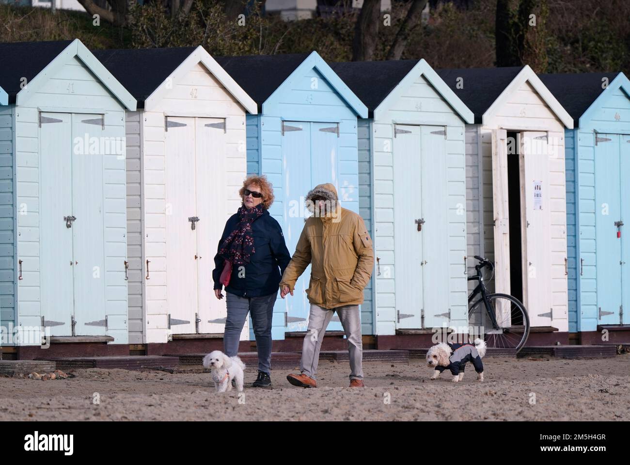 People make their way past beach huts on Avon beach in Mudeford, Dorset ...