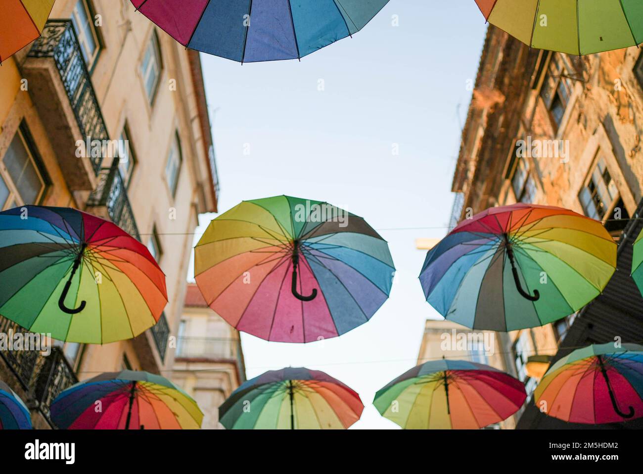 Rainbow colored umbrellas hanging between buildings Stock Photo - Alamy