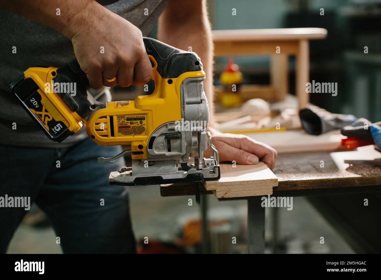 A wood-worker using a jigsaw to cut out a curve in a work piece of pine ...
