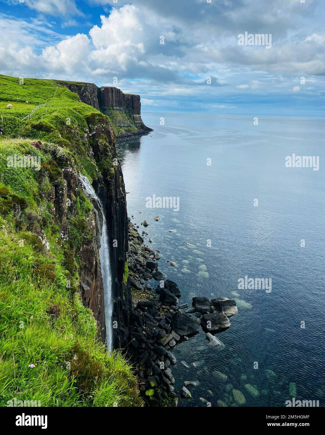 A vertical shot of the Kilt Rocks waterfall flowing down into a sea in ...