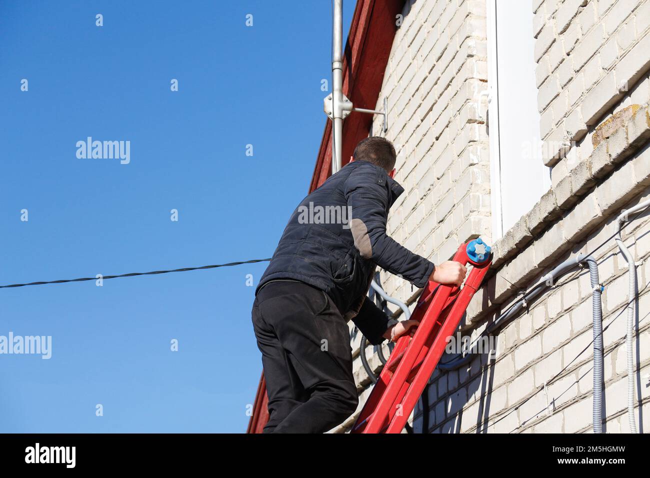 Young man climbing the ladder. Industrial climber in helmet and overall ...