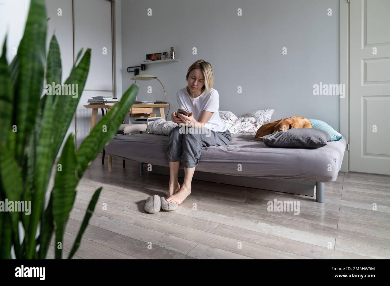 Unhappy pessimistic woman sits on bed with phone in hands waiting for ...