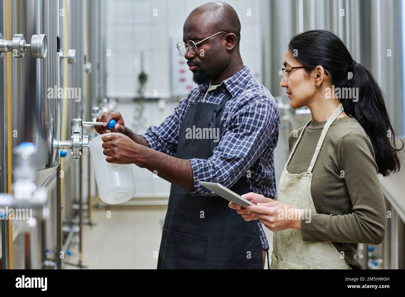 Couple of engineers tasting brewed beer from tank during their work in ...